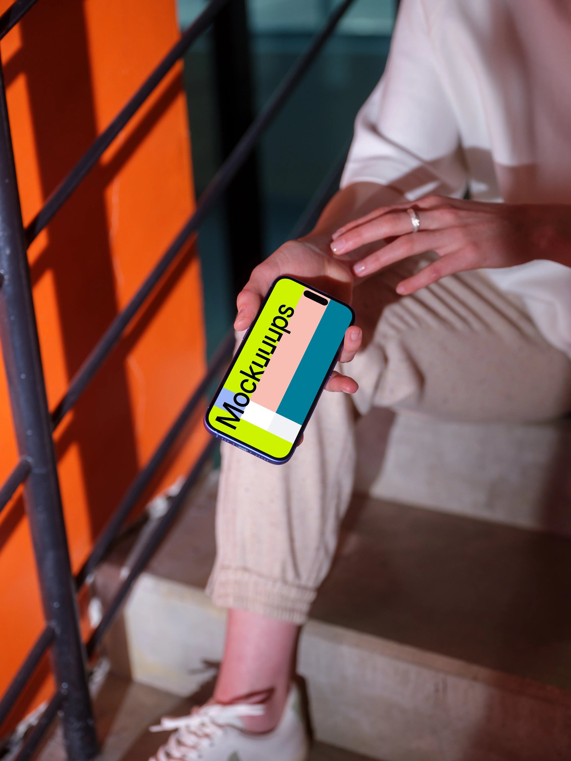 iPhone 16 mockup in a casual hand on concrete stairs - Mockuuups Studio